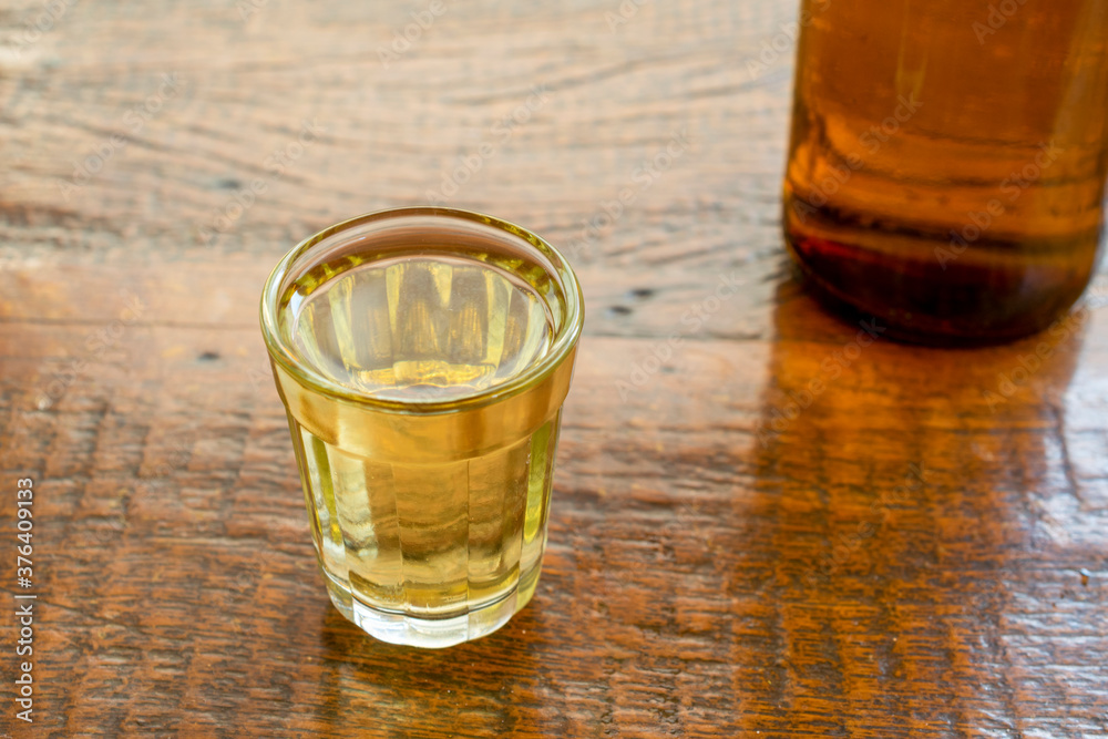glass of golden cachaça and bottle detail on rustic table. Brazilian ...