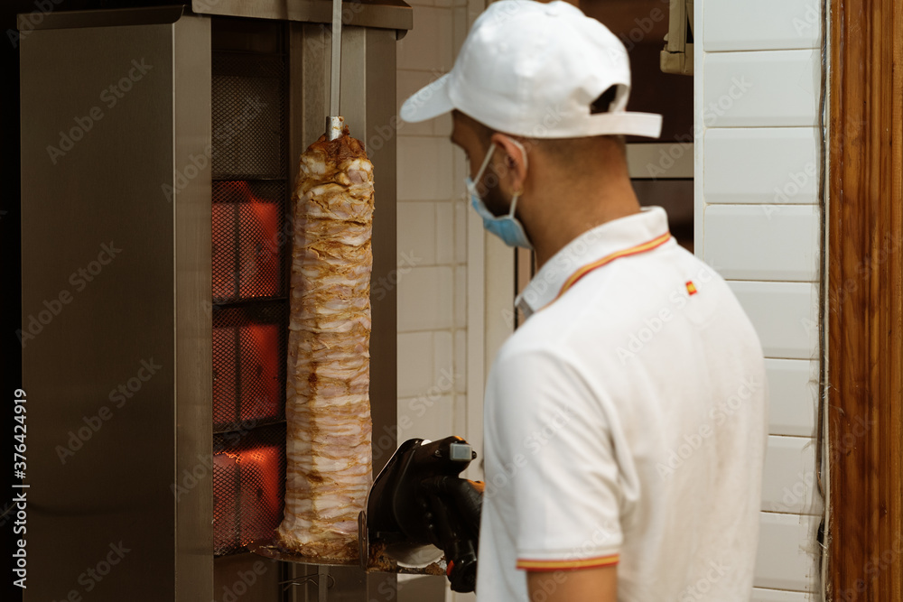 Uniformed chef, cutting and preparing chicken and beef doner kebabs ...
