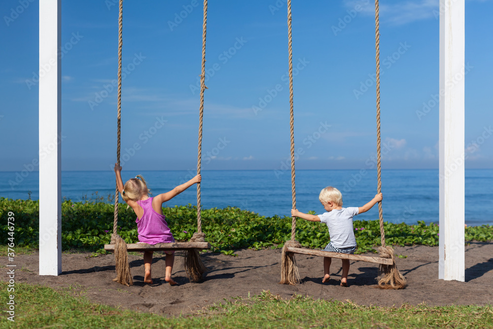 Two happy children have fun swinging high in mid air on rope swing on ...