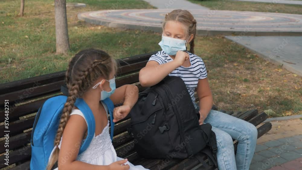 Schoolgirls sit in the park on a bench wearing medical masks and say ...
