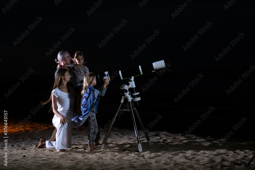 Happy family looking at moon and stars through a telescope at beautiful ...