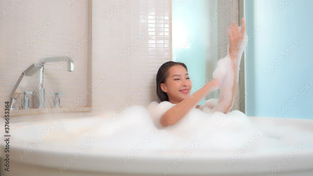 Woman taking a hot bath relaxing in a bathtub filled with foam inside a ...
