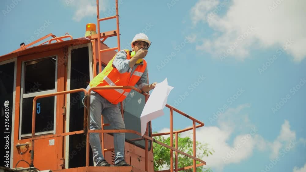 Foreman holding blueprint talking on the walkie-talkie control loading ...
