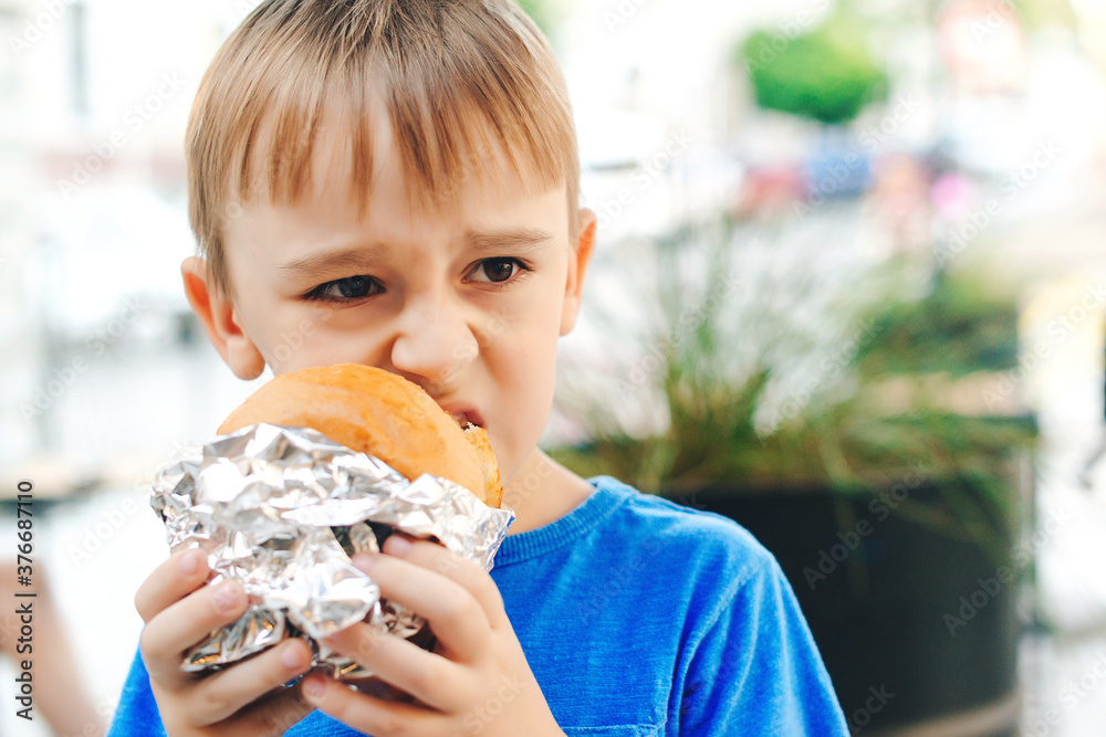 Hungry boy eating a burger at outdoors cafe. Cute child eating fast ...