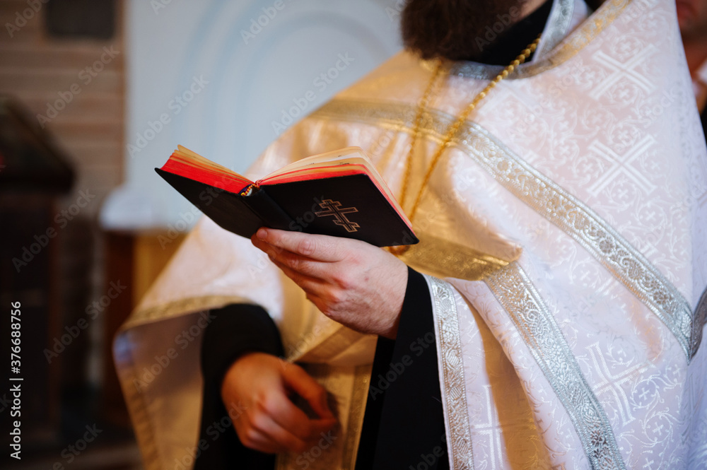 Priest in white church dress reads a small prayer book during a church ...