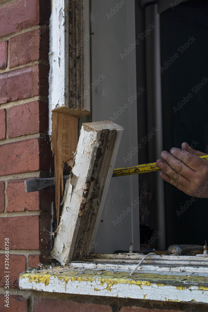 Crowbar being used to remove an old wooden window frame in brick wall ...