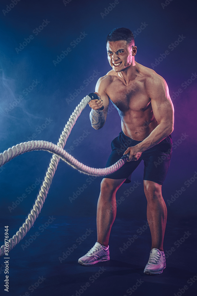 Athletic looking bodybulder work out with battle rope on dark studio ...