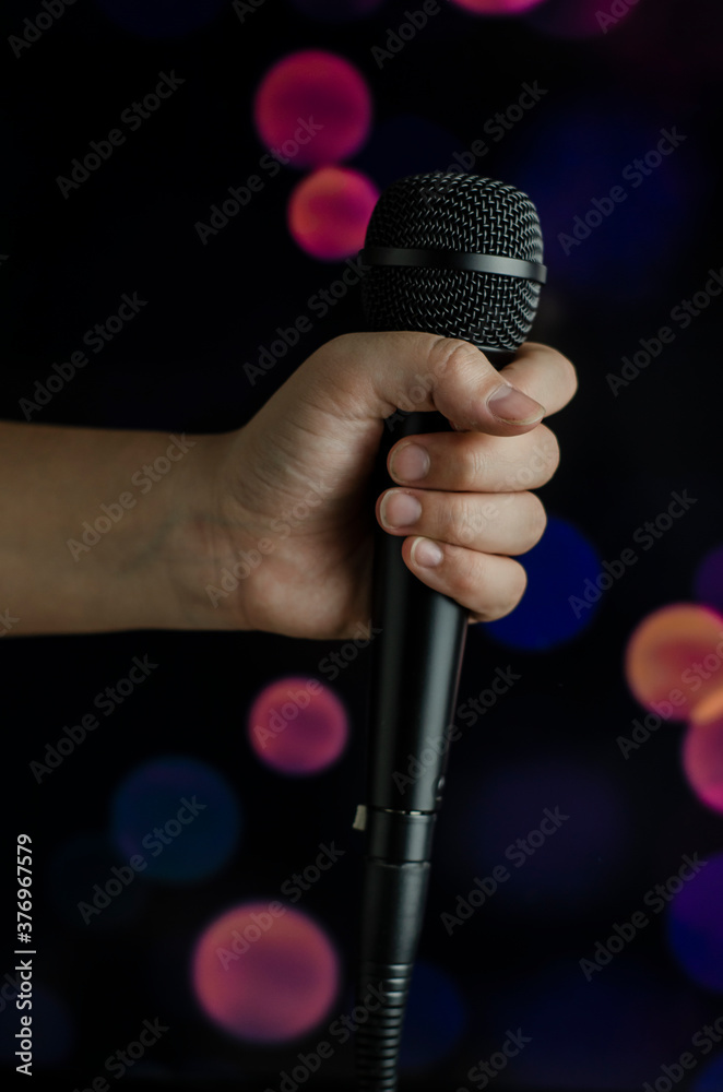mano sosteniendo micrófono color negro con fondo de luces de colores ...