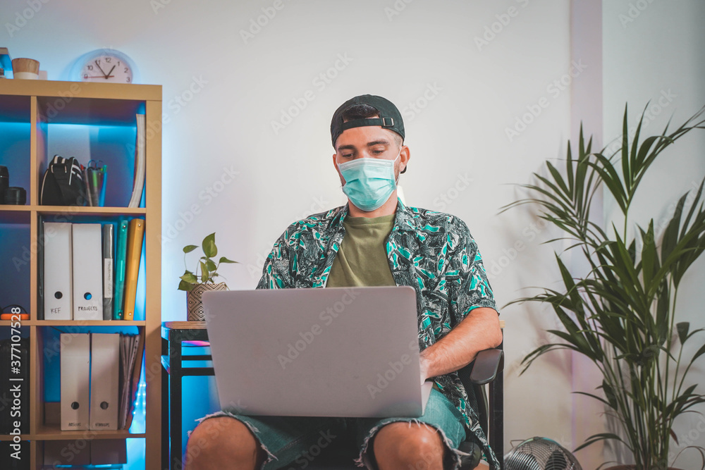 Young man with face mask working from home with laptop. Influencer ...