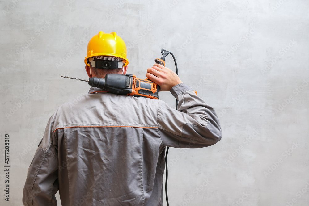 hand of the builder holds an hammer drill on background of gray wall ...