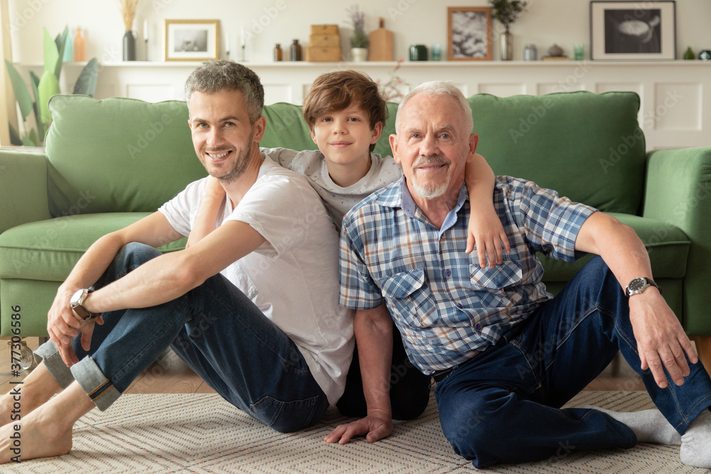Portrait of three generations of men sitting on the warm floor in ...