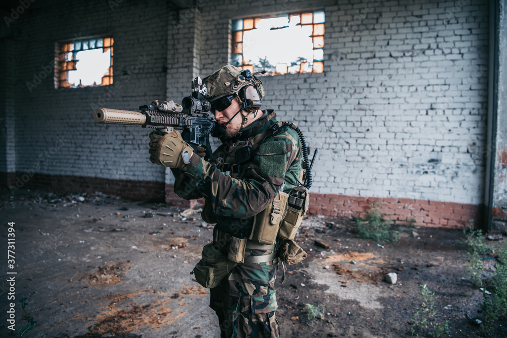 Military man with assault rifle standing inside building, he is ready ...