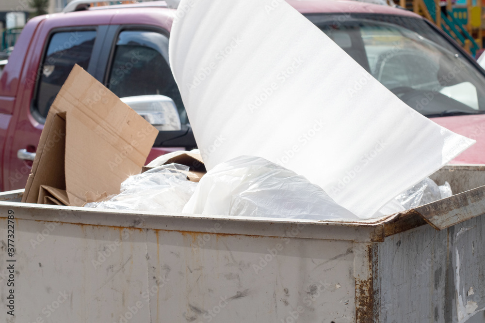 Overflowing trash can on a city street in front of a car. Plastic trash ...