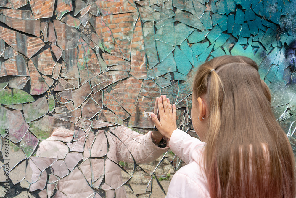 Young girl looks in a broken mirror and shows her hand on a mirror ...
