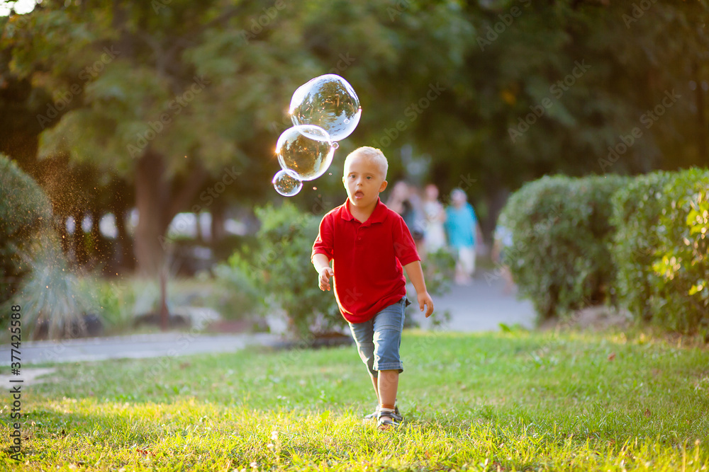 Little cute boy with Down Syndrome plays with huge soap bubbles in the ...