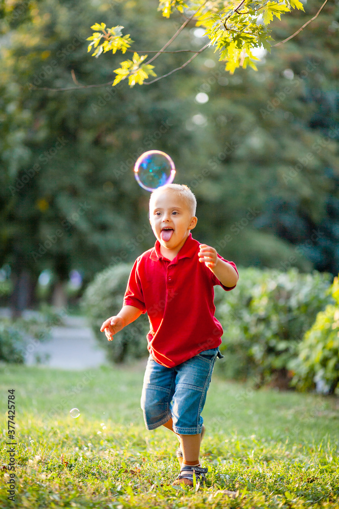 Little cute boy with Down Syndrome plays with huge soap bubbles in the ...