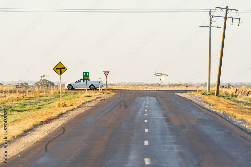 A farm ute passing through a rural T intersection with leaning power ...