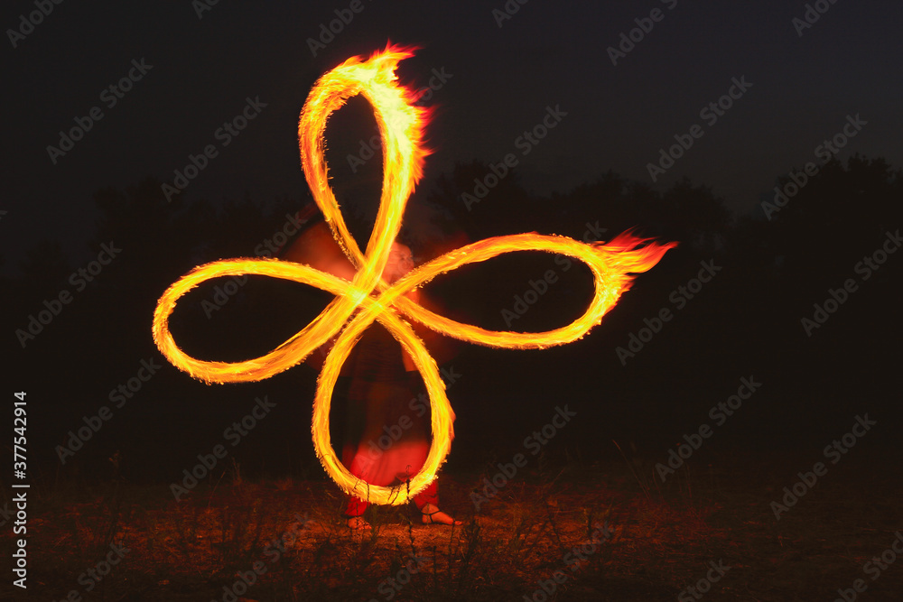 Fire dancer drawing figures by fire at night. Fakir woman turns fire in ...