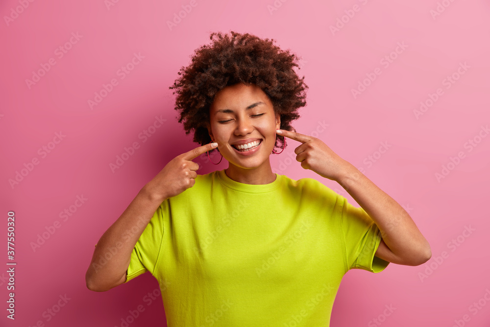 Horizontal shot of overjoyed dark skinned young woman points at her ...