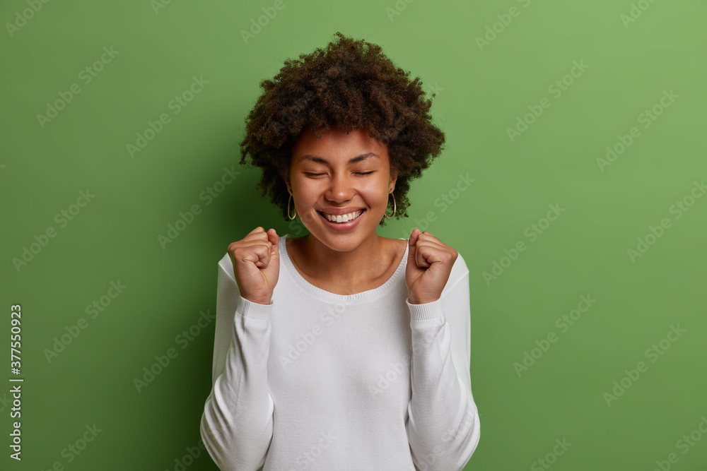 Happy joyous young woman has Afro hair turns out to be winner, holds ...