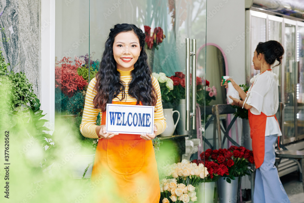 Pretty young smiling flower shop owner welcomming customers inside, her ...