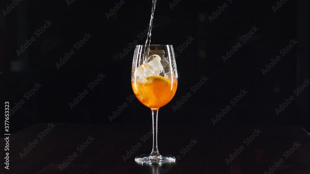 Close up bartenders hands pouring prosecco in wine glass with ice, mixing cocktail with orange ...