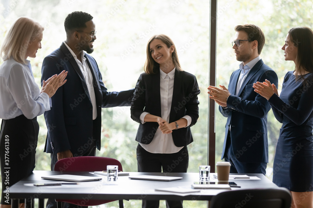 Smiling multiracial businesspeople congratulate young successful female ...