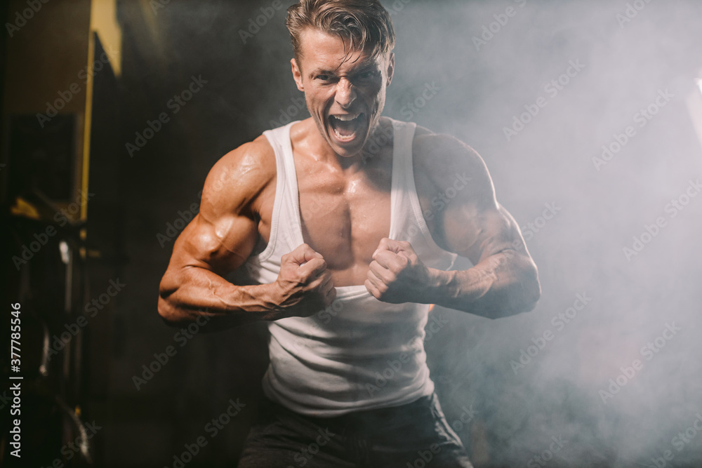 Bodybuilder man pumping muscles and posing in ripped shirt. Hot and ...
