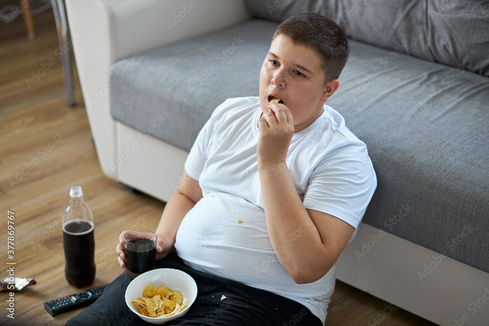 Foto de overweight fat boy eat junk food while watching tv alone at ...