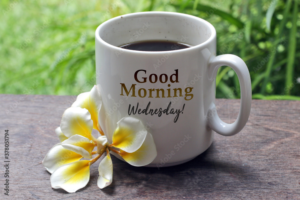 A cup of coffee with Bali frangipani flower on the wooden table with morning text greeting on it ...
