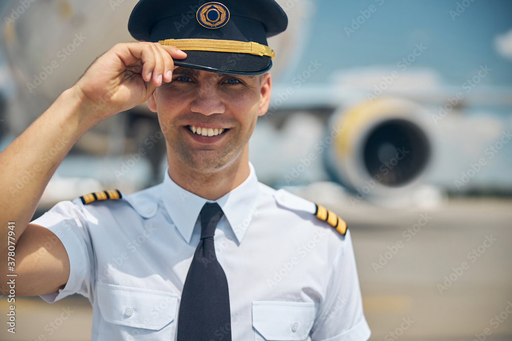 Handsome pilot in command touching captain hat and smiling Stock Photo ...