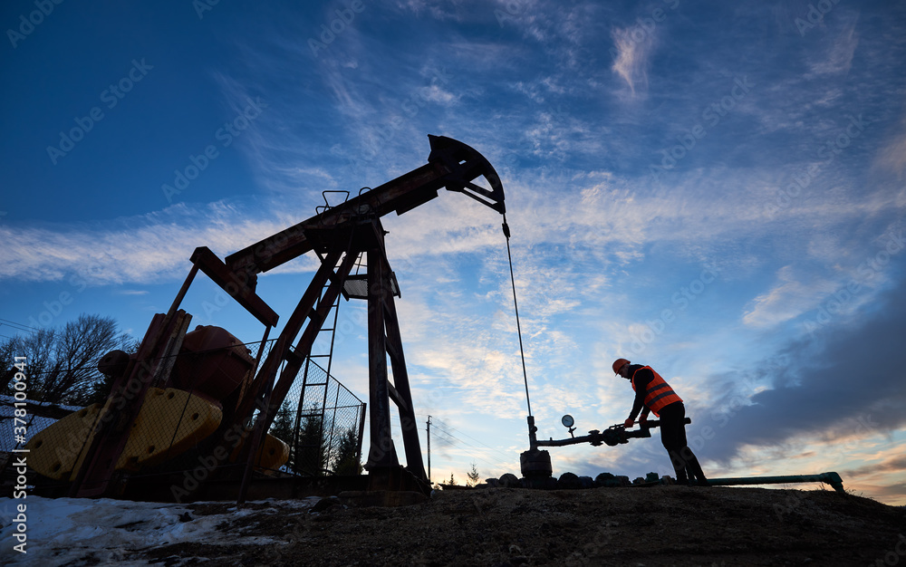 Silhouette of petroleum operator in work vest and helmet using oil ...