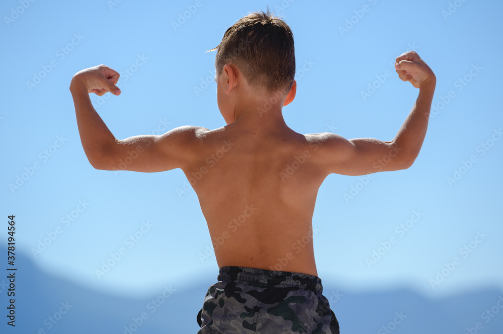 one healthy strong little boy showing back muscles on blue sky and ...