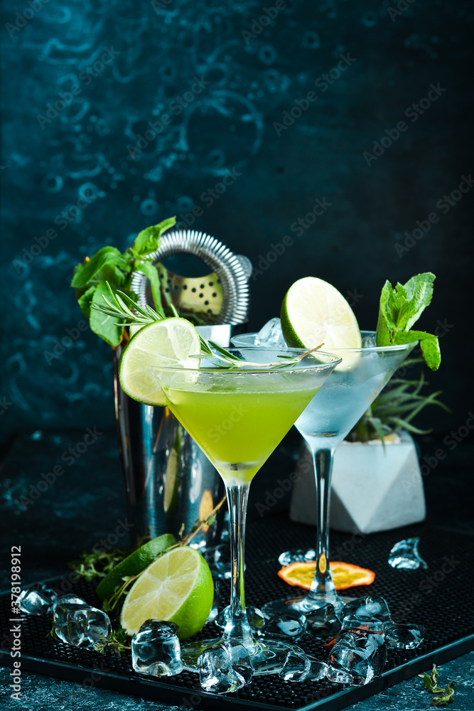Green alcoholic cocktail with lime and rosemary. On a black stone ...