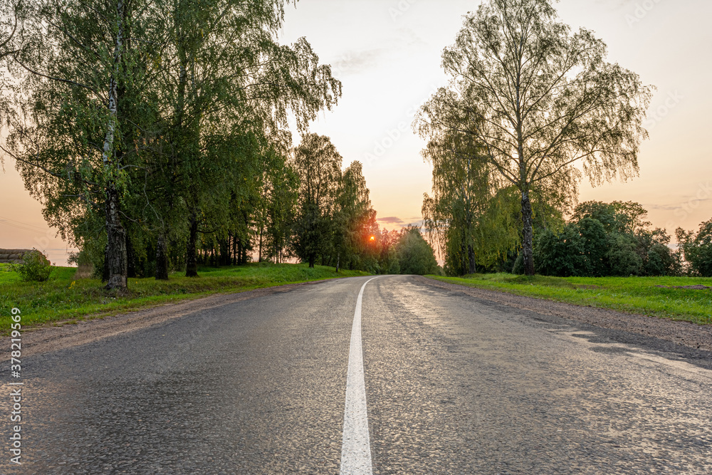 asphalt road in the countryside during sunset, there are big trees on ...