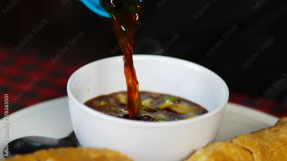 Pouring cuko (sauce of indonesian savory fish cake dish) into a white ...