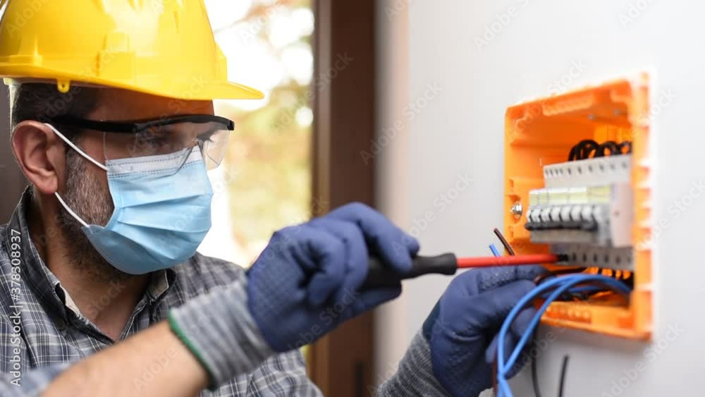 Electrician at work on an electrical panel protected by helmet, safety ...