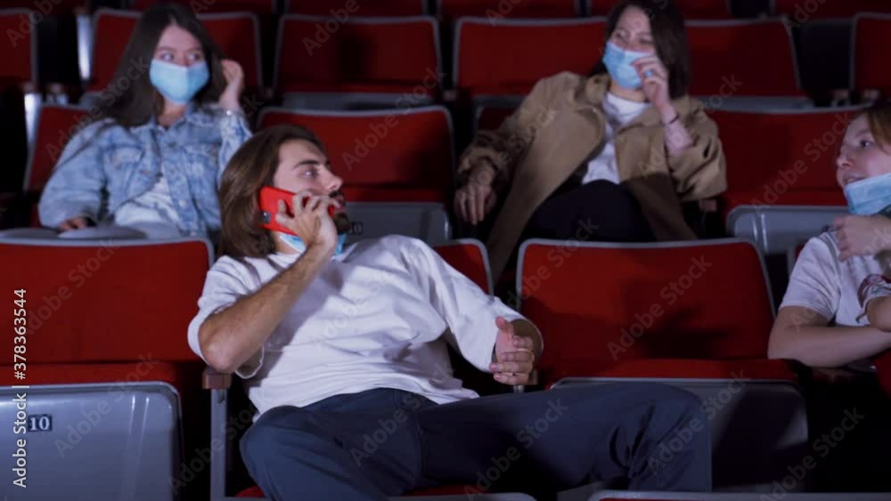Young man talking on phone in movie theater. Media. Impudent man is ...