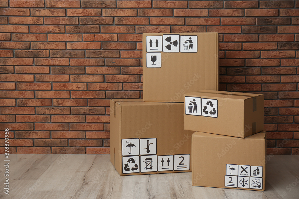 Cardboard boxes with different packaging symbols on floor near brick ...