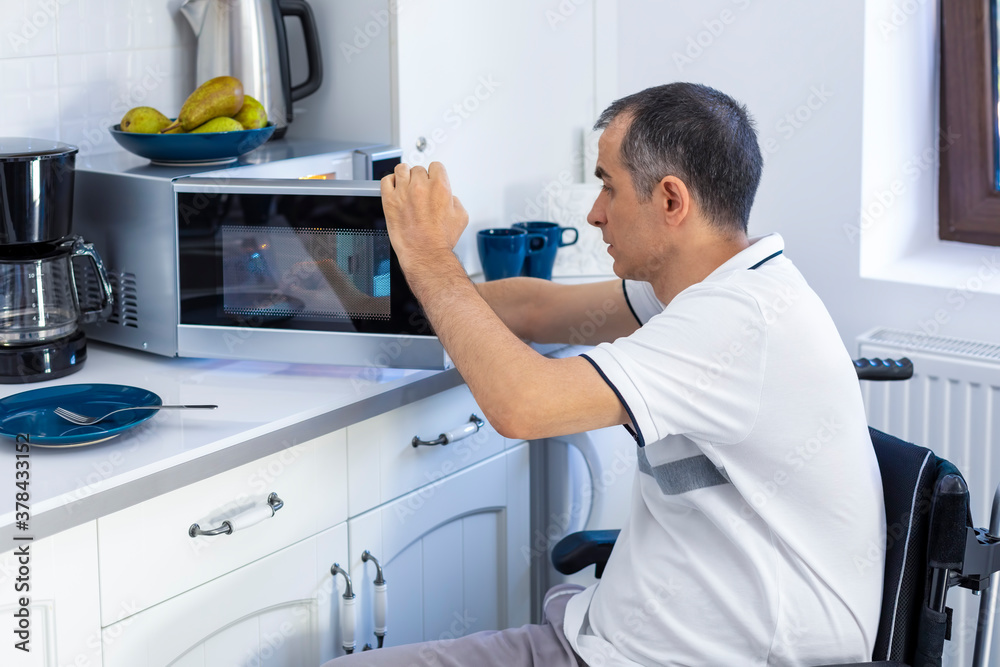 Disabled man in wheelchair using microwave oven for baking in the ...