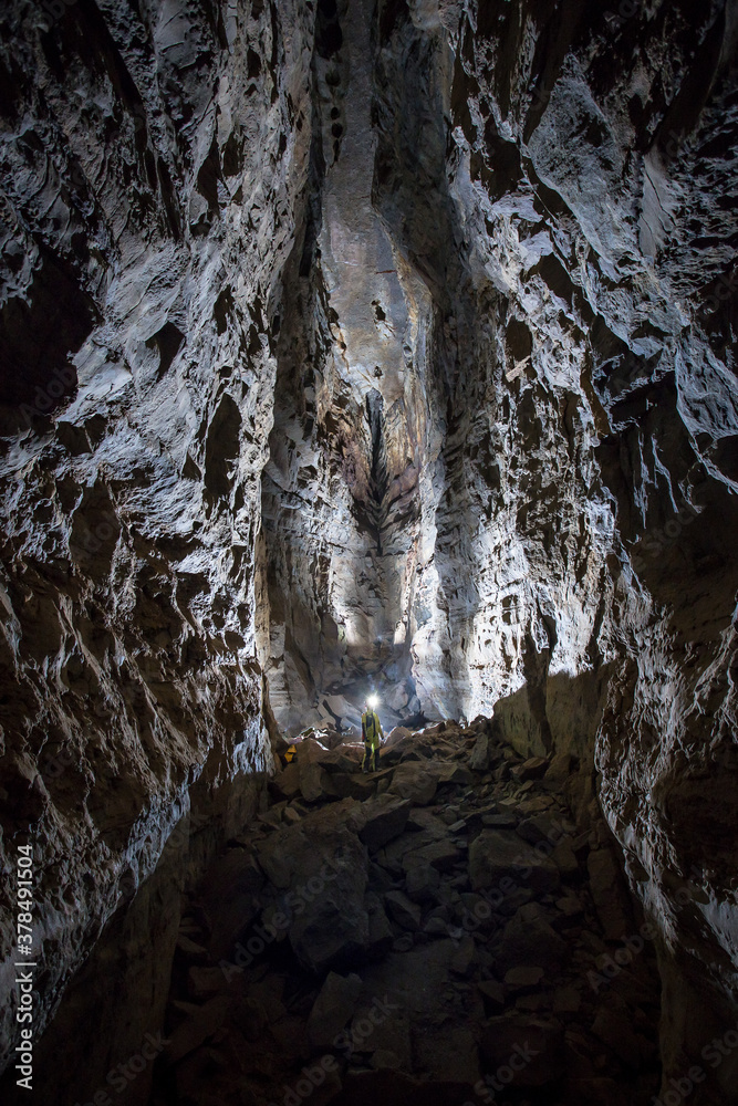 Speleologist in the cave in huge underground hall with light caving ...