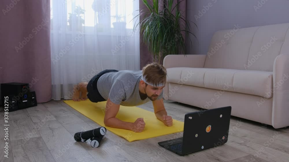 A young, purposeful man does plank exercises on a laptop computer ...