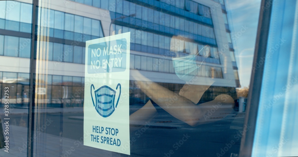 Female wearing face mask placing COVID-19 face mask poster on a window ...