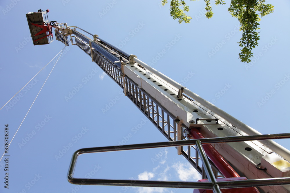 Foto de Tall telescopic fire ladder close up in perspective on blue sky ...