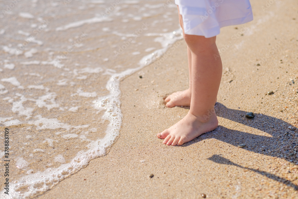 Small baby feet close-up on the sand of the sea beach. Sea water washes ...