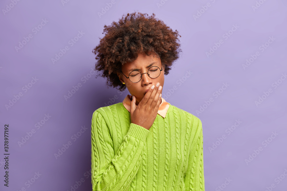 Sleepy tired woman with Afro hair covers mouth and yawns keeps eyes ...