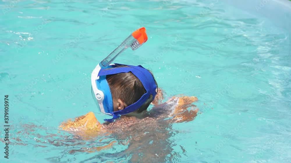 Happy boy in armbands and water mask swims under water in the pool ...