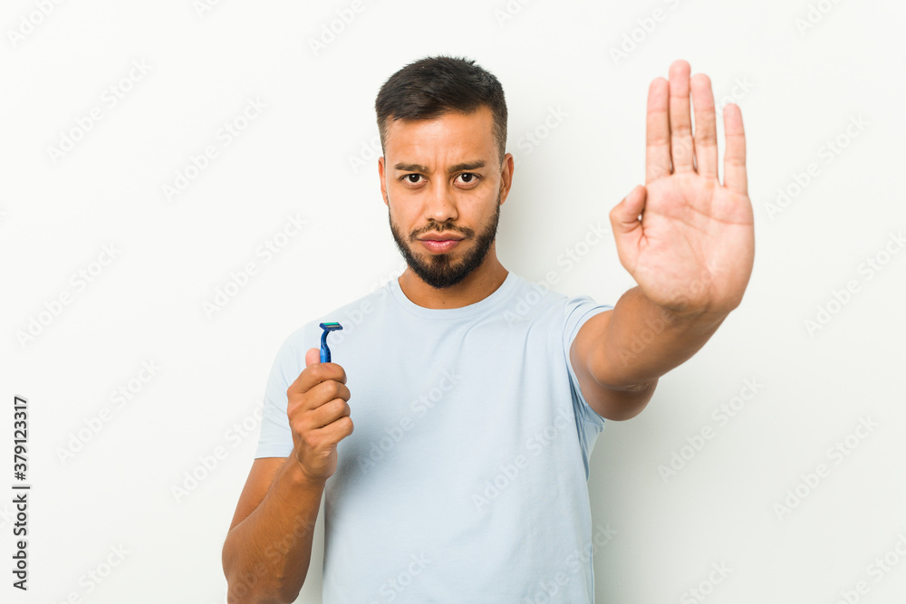 Foto de Young south-asian man holding a razor blade standing with ...