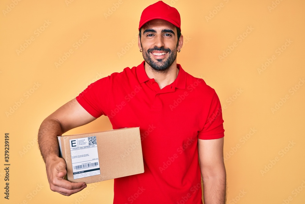 Handsome hispanic man with beard holding delivery package looking ...