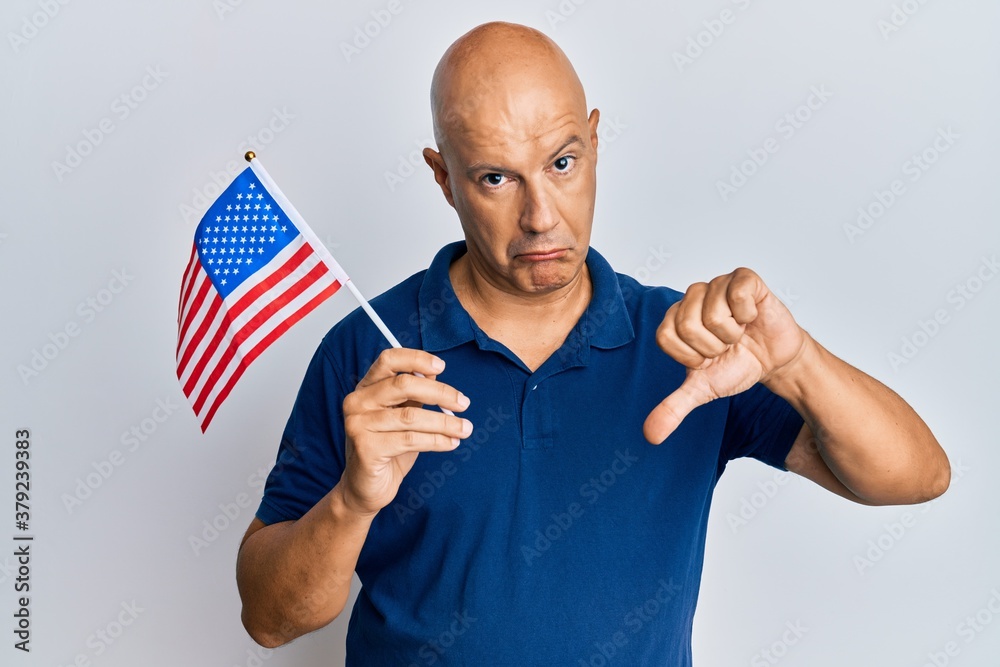 Middle age bald man holding united states flag with angry face ...
